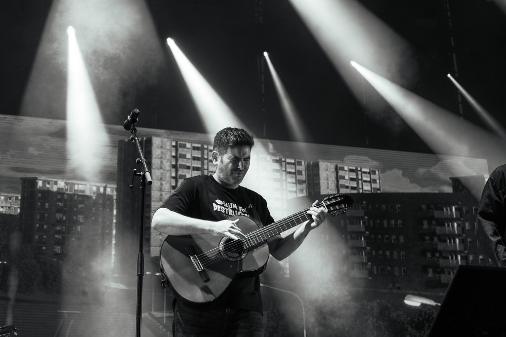 Guitarist on an urban-themed stage under dramatic spotlights (black-and-white)