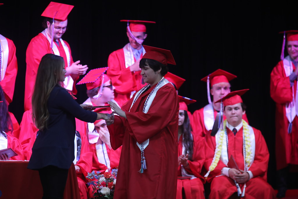 Bayfield 2025 Graduation Ceremony: Diploma Exchange on Stage Among Red Caps and Gowns
