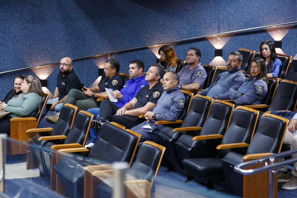 Municipal council session in Itajaí: uniformed officers and civilians in a blue-walled chamber during a public meeting