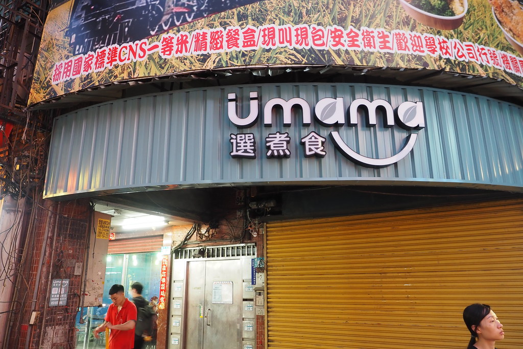 Umama storefront signage over a corrugated metal facade with a yellow rolling shutter — a street-level portrait of urban commerce
