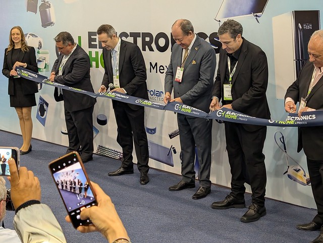 Executives in suits cut a ribbon at Electronics Home Mexico trade show; attendees in the foreground film the moment with smartphones.