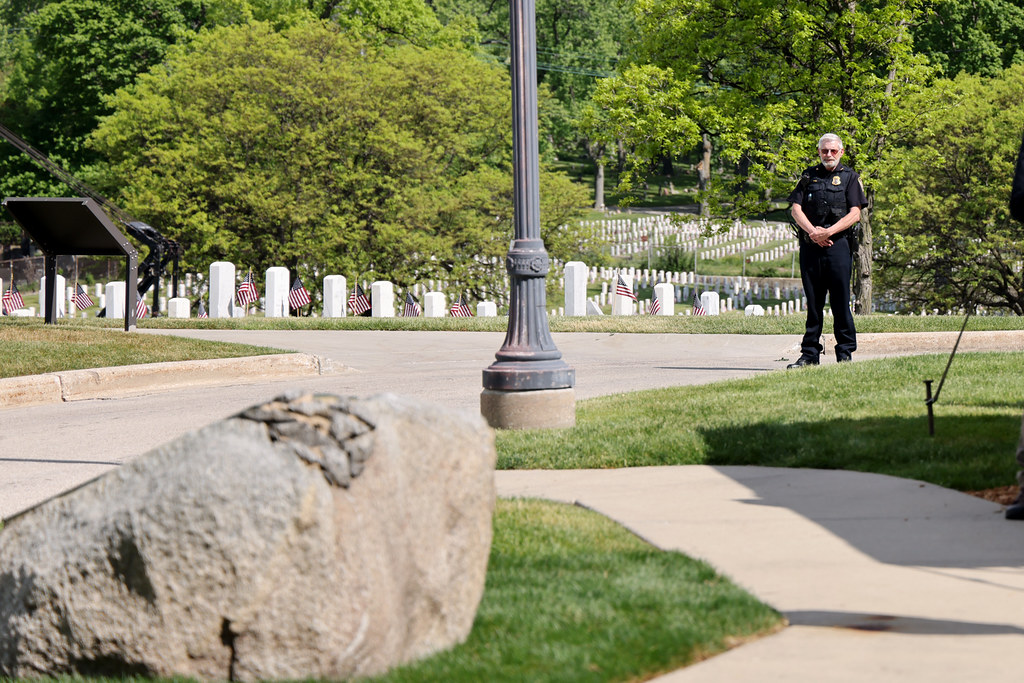 Security officer stands watch during Memorial Day tribute at Wood National Cemetery, Milwaukee VA, among rows of headstones and flags