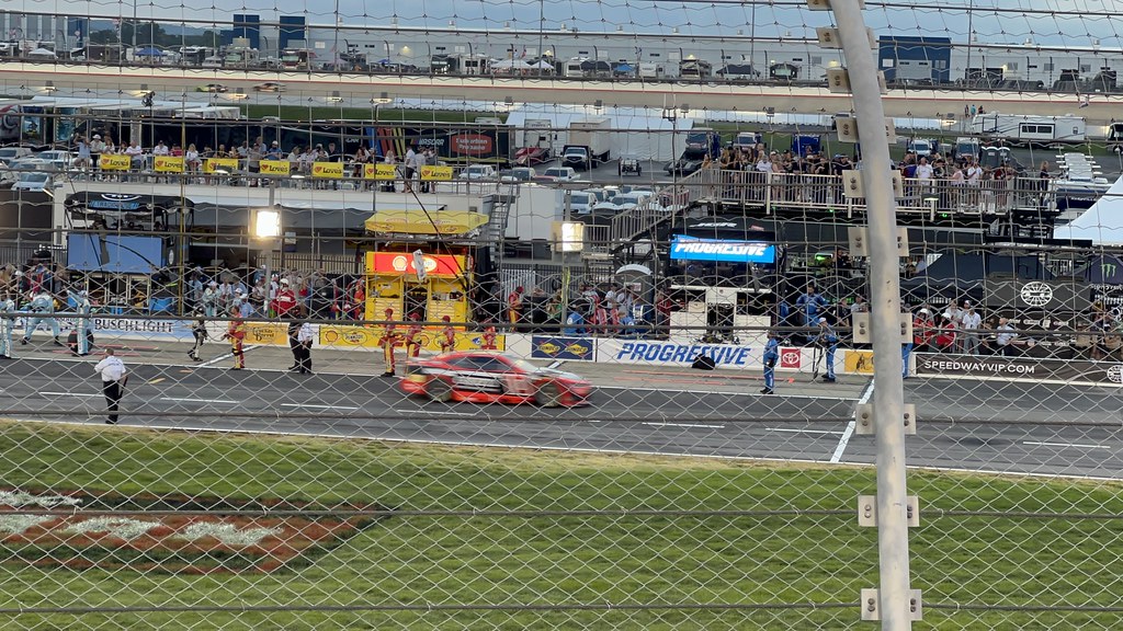 Cracker Barrel 400 (2026) – NASCAR Cup Series Pit Lane: Red Car in Motion Framed by Chain-Link Fence