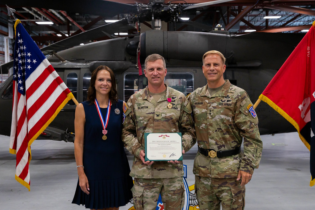 Certificate Award Ceremony in a Military Hangar: Soldier Receives Recognition Amid Teammates with American and Unit Flags