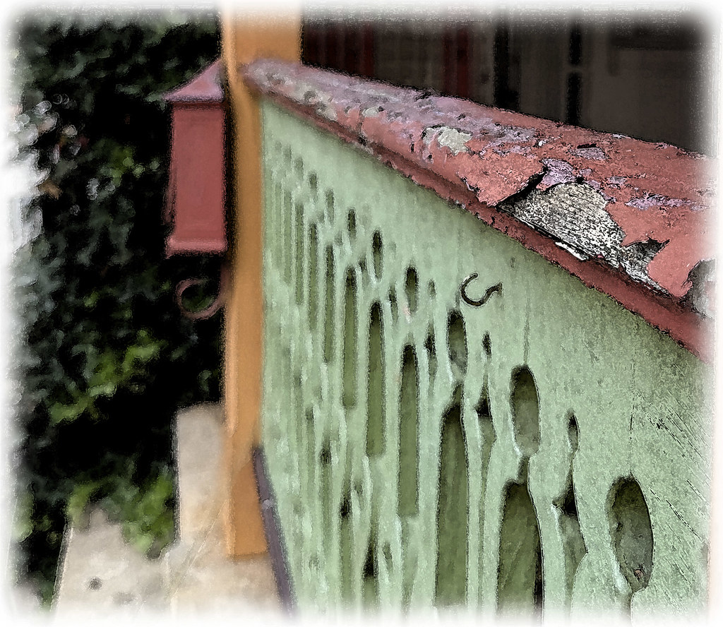 Weathered sage-green railing with peeling rust-red cap and circular cutouts, Mt. Washington, Baltimore