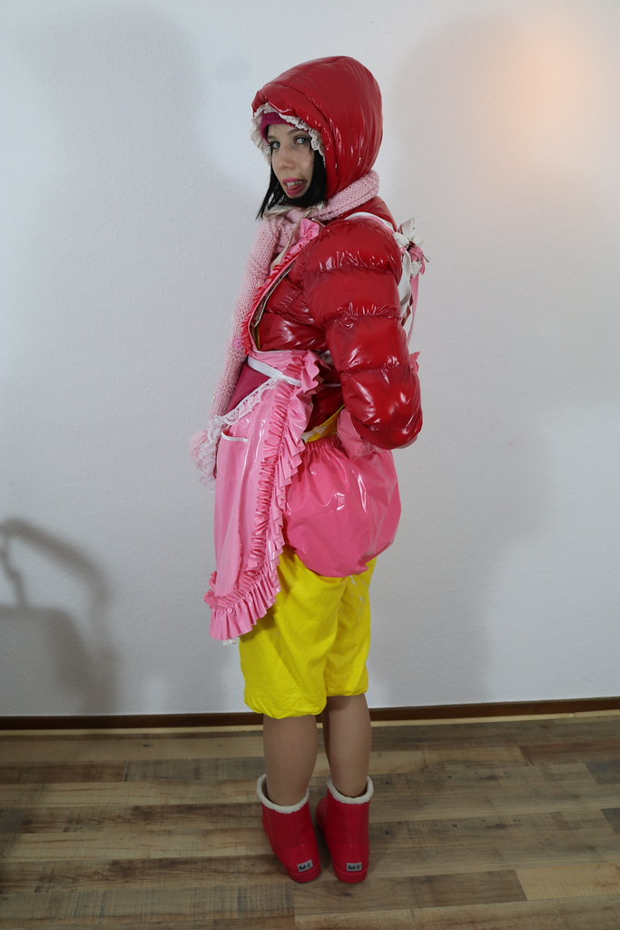 Color-blocked winter fashion portrait: red hooded puffer, pink frilled apron, and yellow shorts