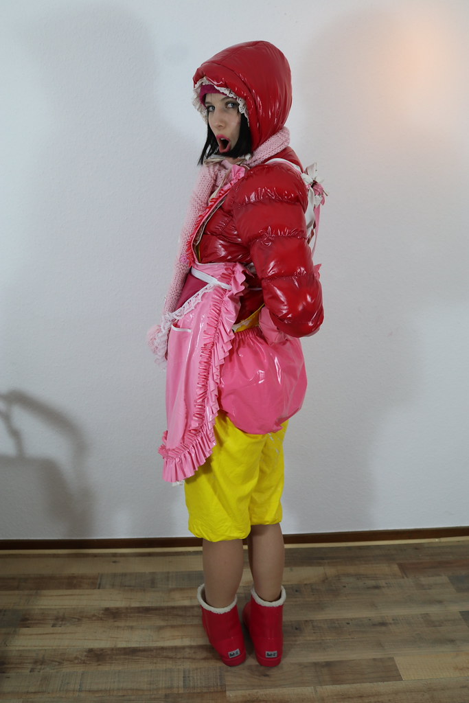 Playful winter-fashion portrait: glossy red puffer, pink ruffled apron, and yellow shorts