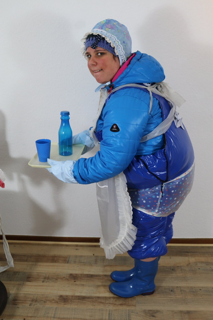 Indoor portrait of a person in a bright blue inflatable winter costume with bonnet, holding a serving tray with a blue bottle and cup