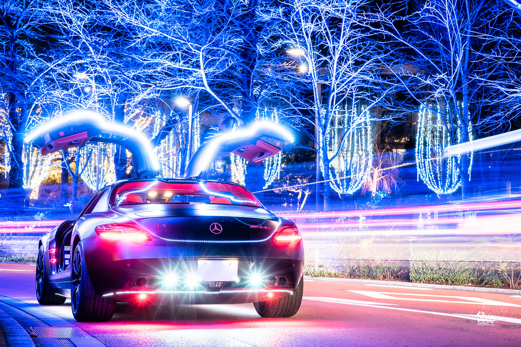 Mercedes-Benz SLS AMG Gullwing in neon-lit urban night, blue-lit trees, and light-trail streaks