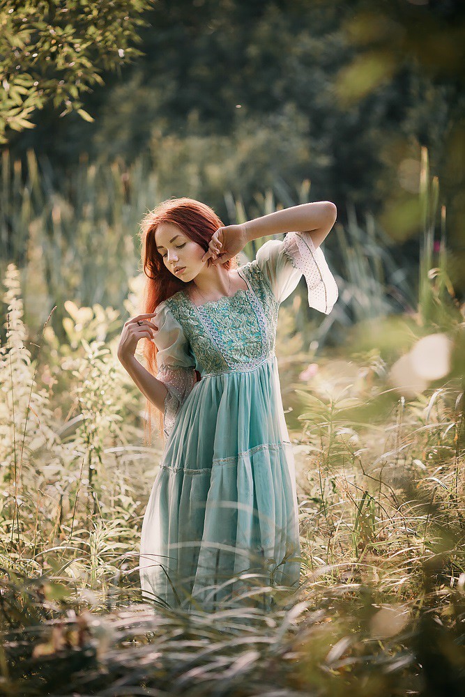 Golden-hour portrait in a sunlit meadow: woman with red hair in a flowing turquoise lace dress