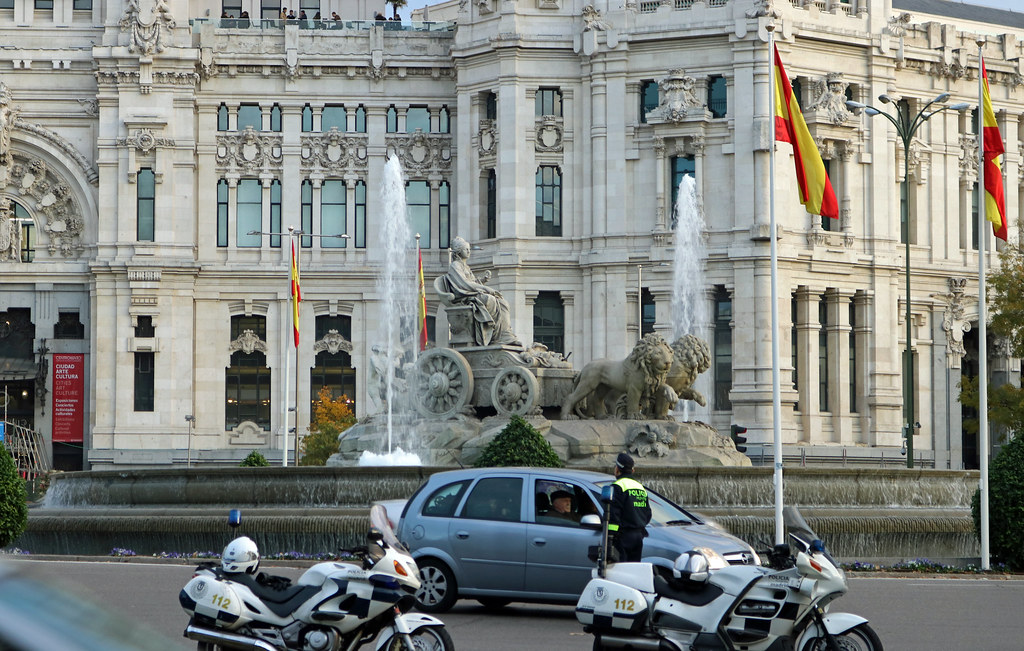 Fuente de Cibeles in Madrid's Plaza de Cibeles — Neoclassical fountain with lions, flags, and urban traffic
