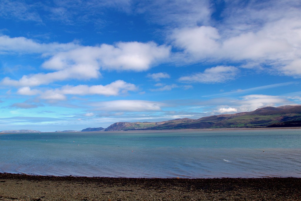 Edge of the Menai Strait: Beaumaris shoreline with turquoise water and rolling Welsh hills under a bright sky