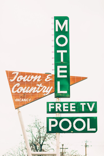 Vertical green MOTEL sign with left orange Town & Country sign; green panels read FREE TV and POOL; bare trees and utility poles in background.