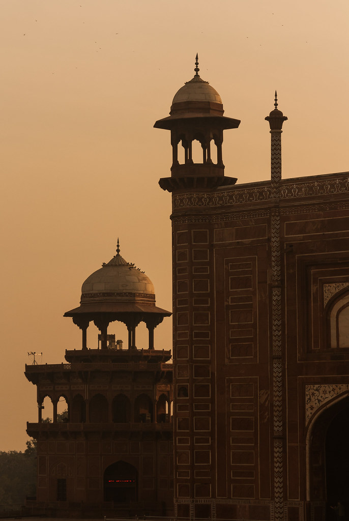 Sunset silhouette of a Mughal-era sandstone gateway with domed pavilions and ornamental inlays