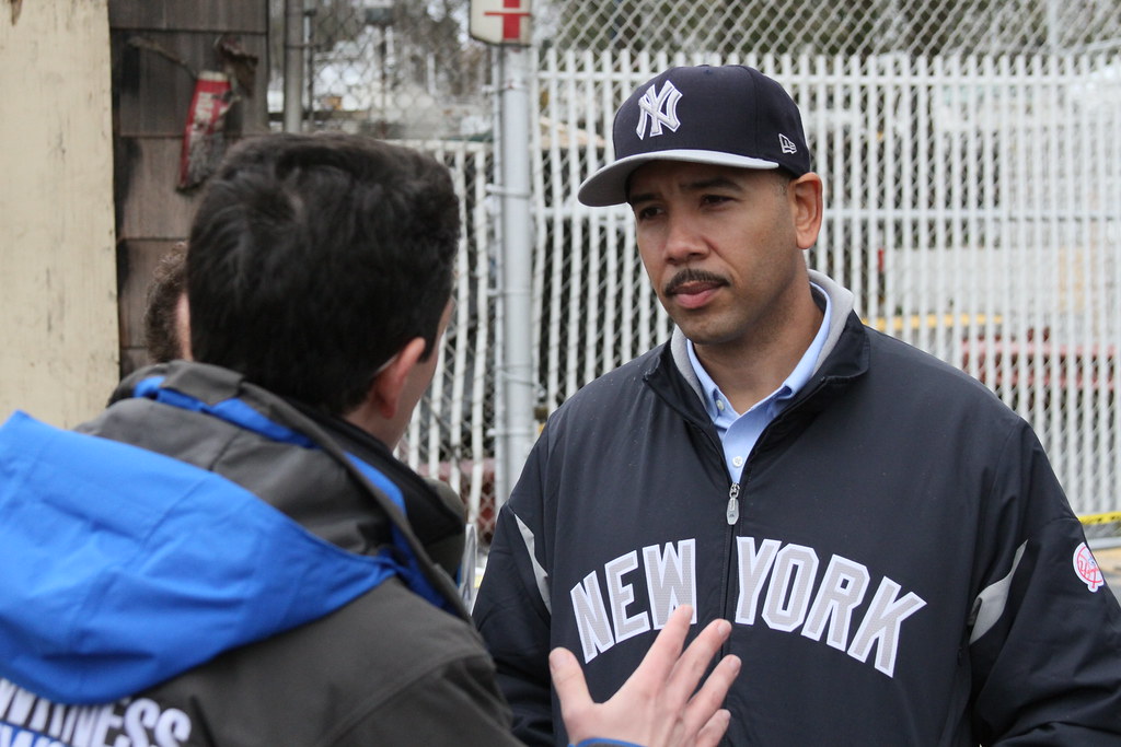 On-site dialogue by a construction fence: man in a New York Yankees cap talks with a colleague