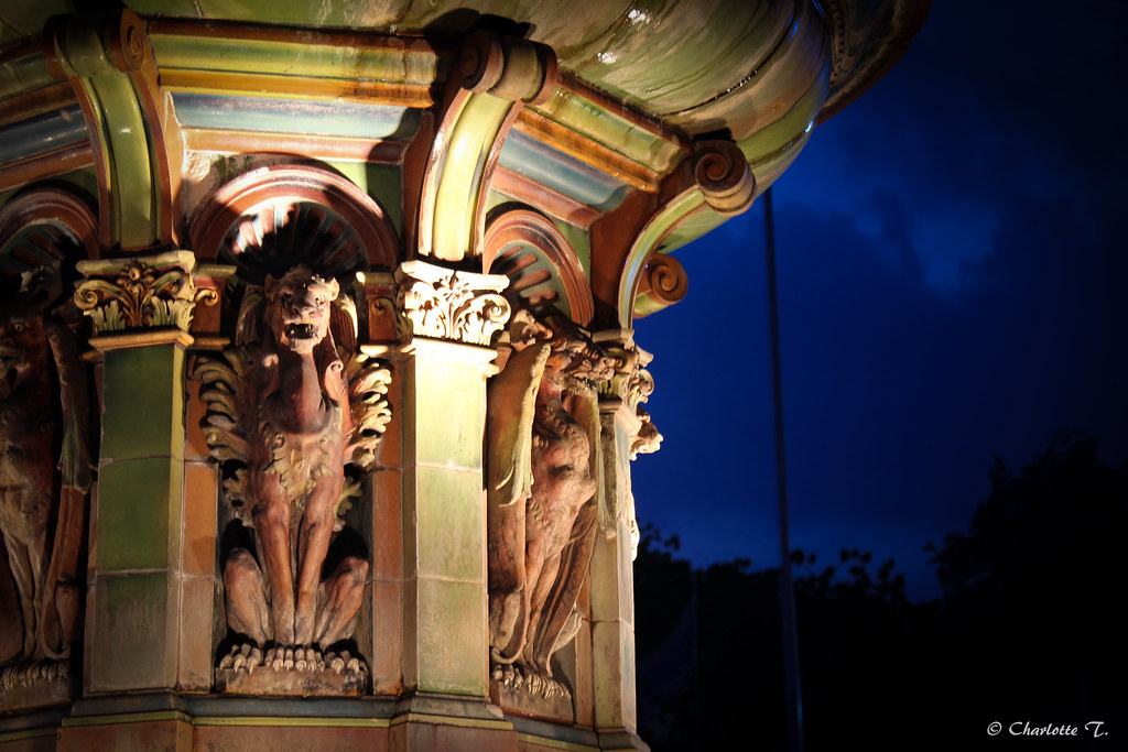 Illuminated capitals and lion figures on an ornate pavilion at night