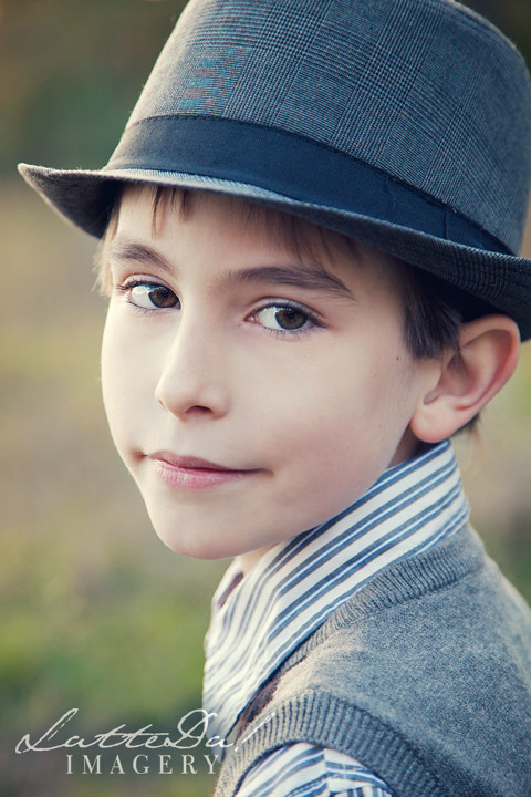 Portrait of a boy in a vintage fedora with a striped shirt, captured in soft outdoor light