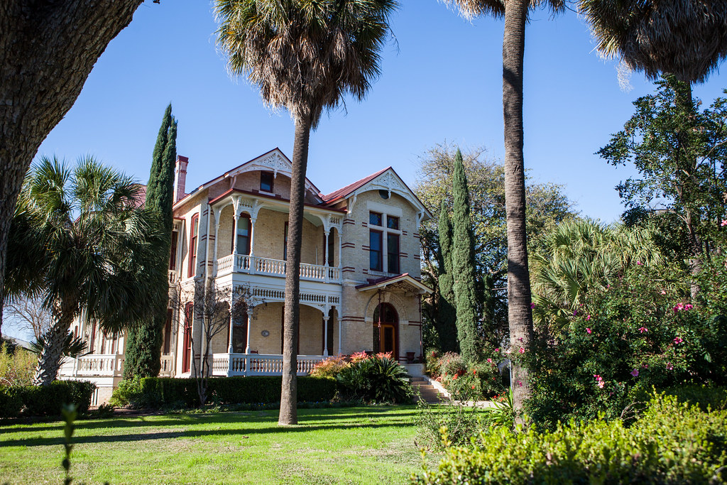 Sunlit Victorian villa with wraparound porch amid towering palms