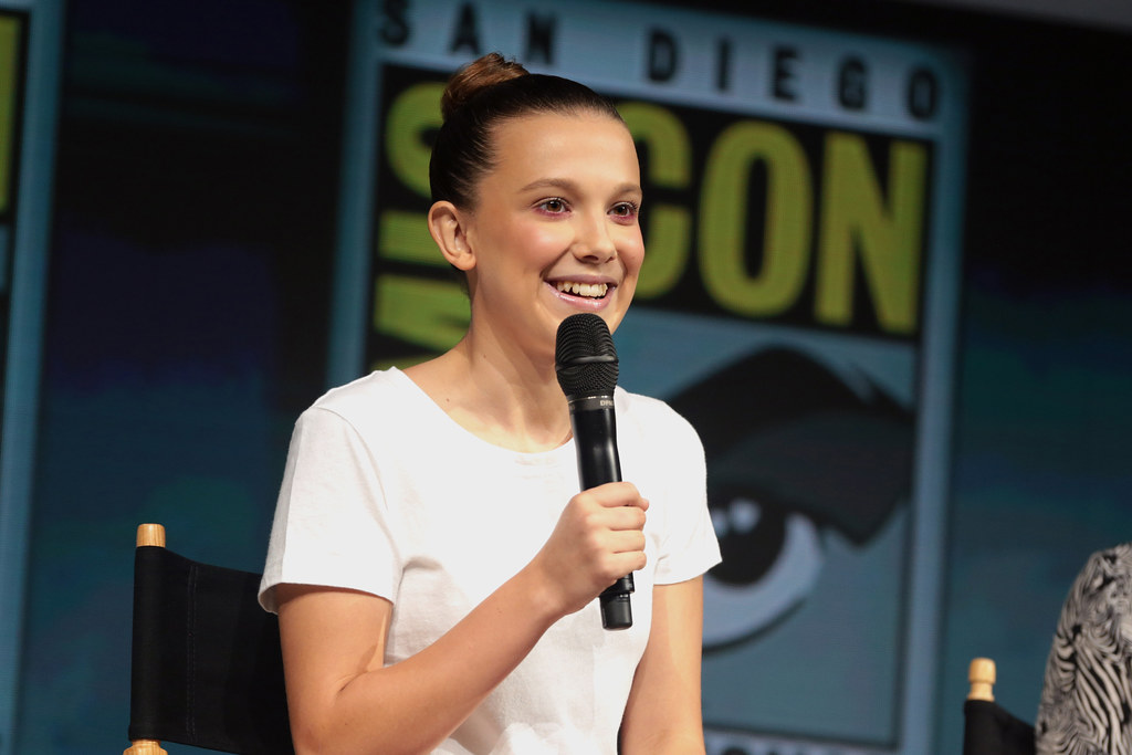 Onstage at San Diego Comic-Con 2018: Speaker in a white T-shirt holding a handheld microphone during a panel