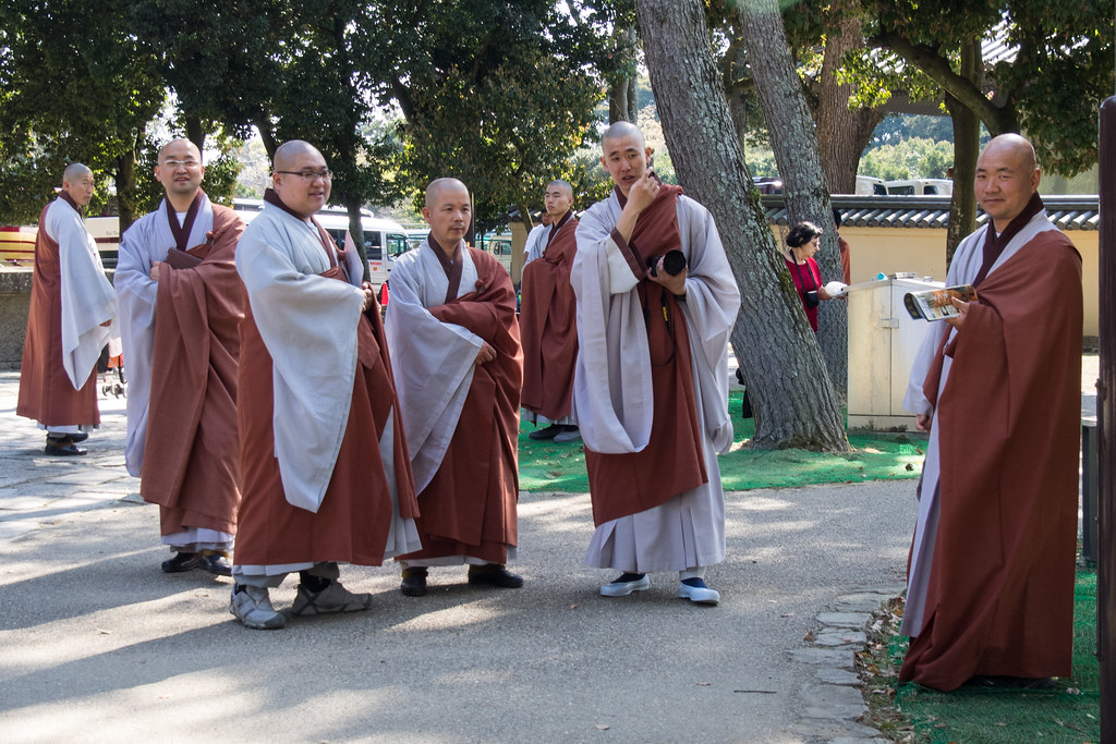 Monks in traditional robes gather along a gravel path at a temple complex in Nara, Japan