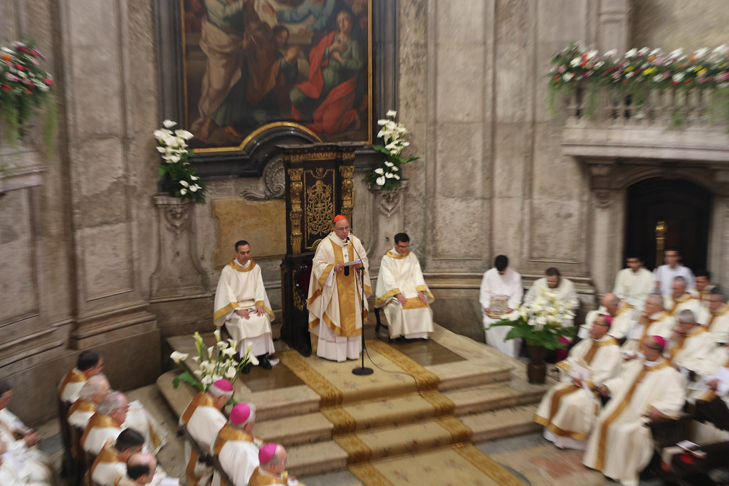 Cardinal presides from a raised lectern during Missa Crismal (Holy Oils Mass) as bishops surround him in Lisbon's Patriarchal Cathedral