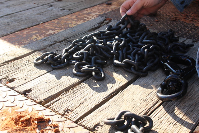 Close-Up of Interlocking Chains on Weathered Wood with a Hand Reaching for a Link